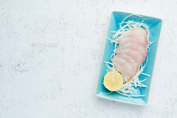 Sashimi from slices of raw white fish fillet on a blue plate on a white ...