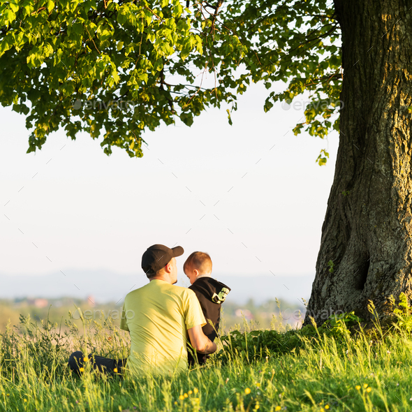 Dad with son in the spring meadow sitting under the tree Stock Photo by ...