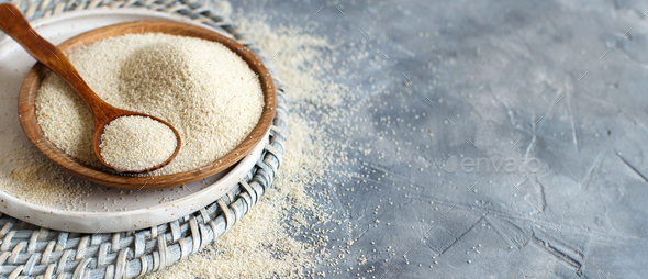 Raw uncooked fonio seeds with a spoon on a plate on grey background ...