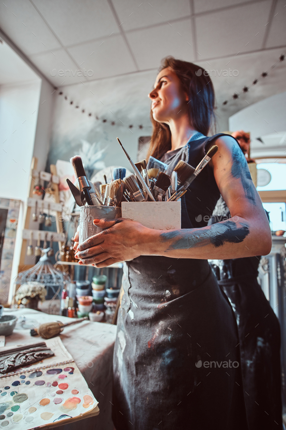 Young attractive painter is posing with brushes in her own cozy ...