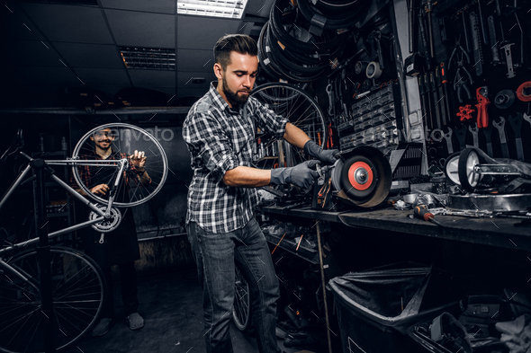 Attractive man is working with machine at busy bicycle workshop. Stock ...