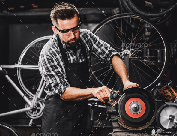 Repairmaster is working with machine tool at busy bucycle workshop ...