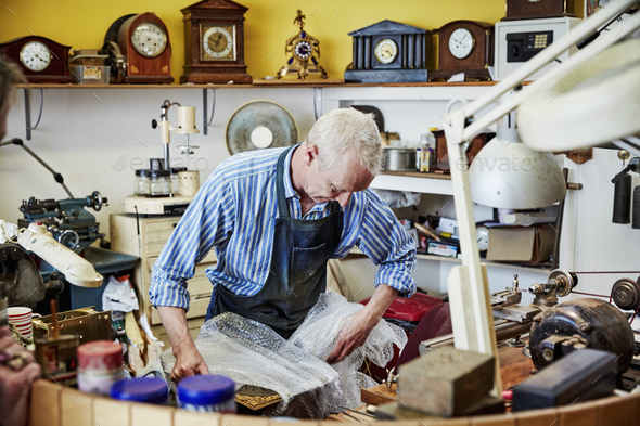 A clock maker busy in his workshop wrapping an antique clock. . Stock ...