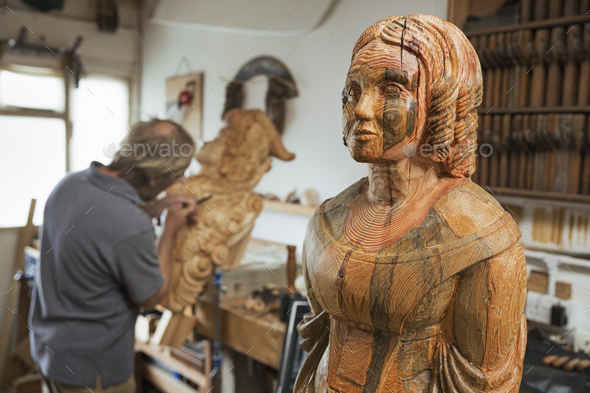 A craftsman working on a wooden ship's figurehead in a workshop using a ...