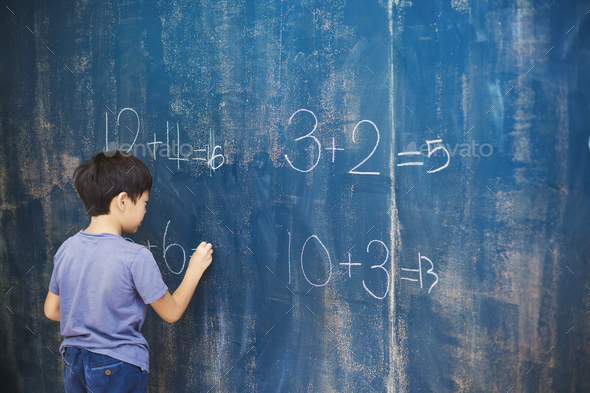 A group of children in school. A boy writing in chalk on a chalkboard ...
