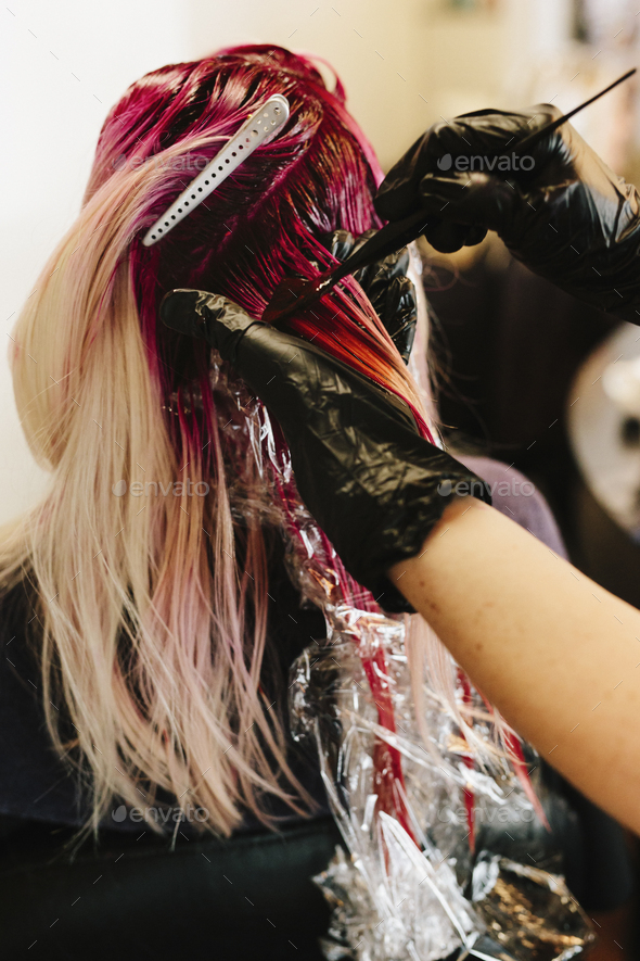 A hair colourist applying pink hair colour to a client's long blonde ...
