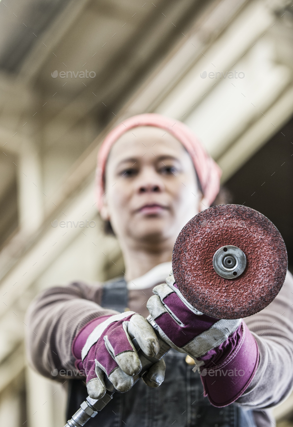 Black woman factory worker using a metal grinding tool in a sheet metal ...