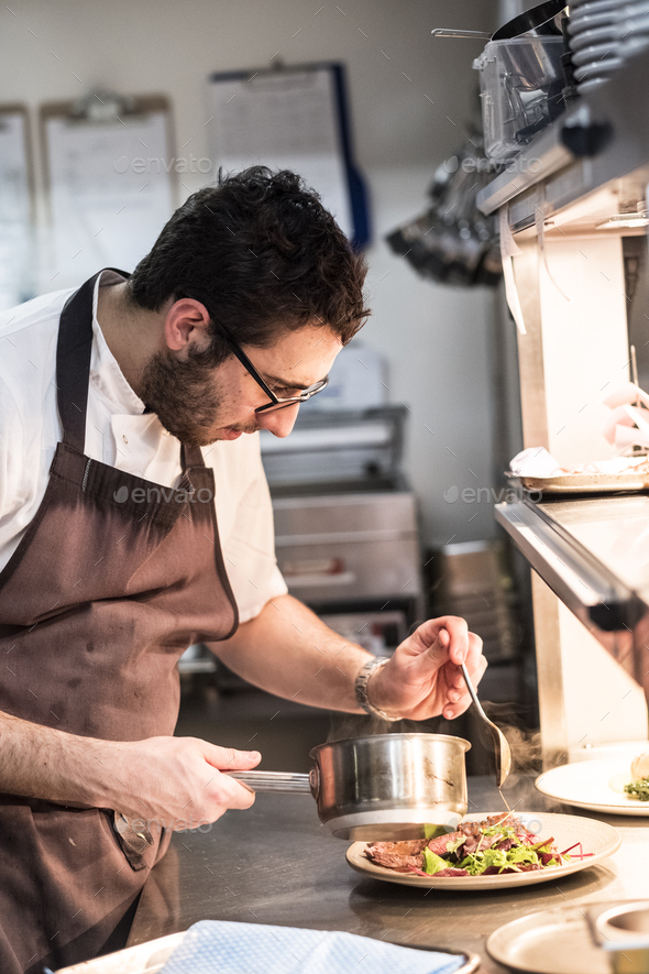 Bearded chef wearing glasses and apron standing in commercial kitchen ...