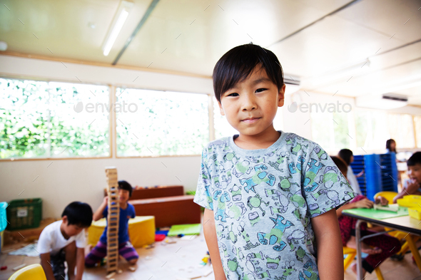 Young boy standing in a classroom in a Japanese preschool, smiling at ...
