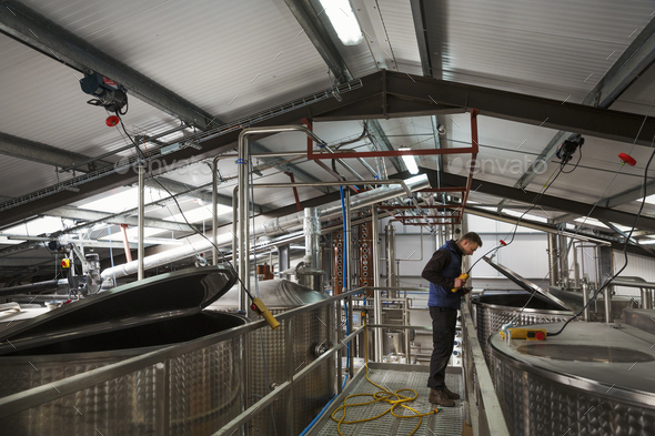 Man checking large metal tanks in a distillery or brewery, lifting the ...