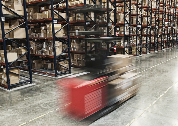 Blur of a motorized stock picker between aisles of cardboard boxes on ...
