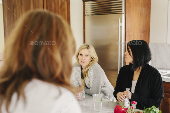 Three women talking together in a kitchen Stock Photo by Mint_Images