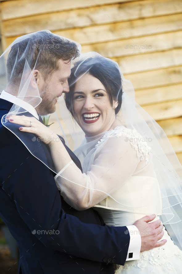 A bride and groom, a young woman laughing and draping her veil over her ...