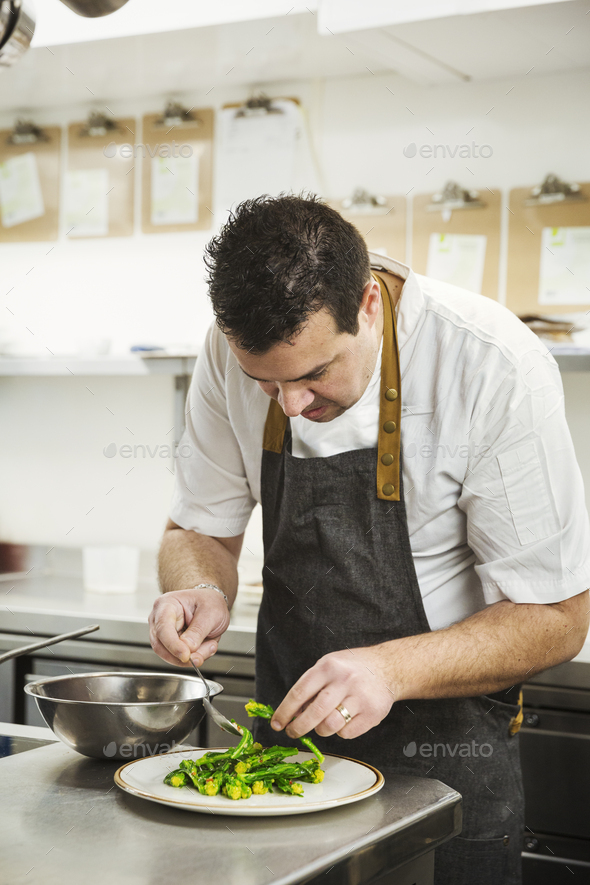 Chef standing in the kitchen in a small hotel, plating up a dish of ...