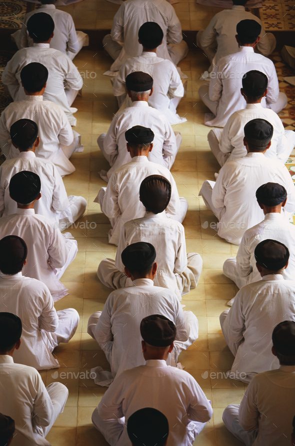High angle rear view of of men wearing white robes sitting in rows on ...