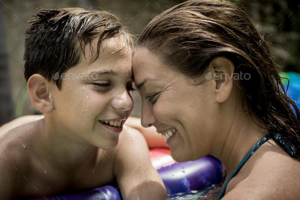 A woman and a boy cuddling in a swimming pool. Stock Photo by Mint_Images
