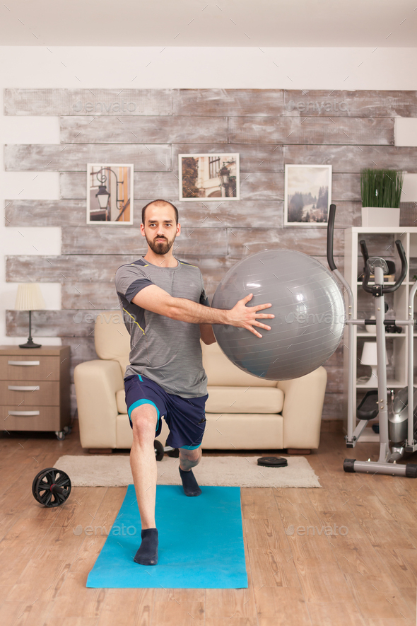 Fit man doing lunges on yoga mat using swiss ball Stock Photo by DC_Studio