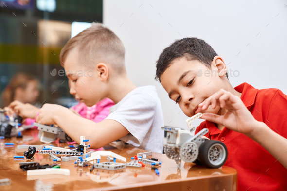 Children creating toys using building kit Stock Photo by serhiibobyk