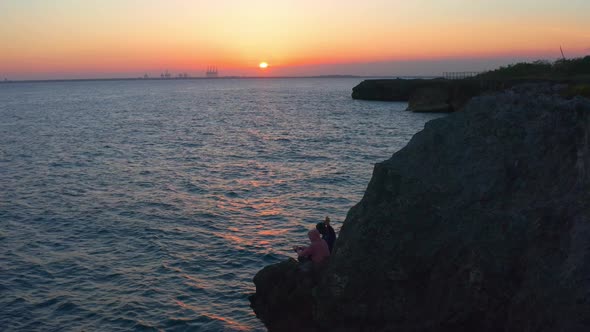 Aerial view of two Dominican greeting fishermen sitting on cliff with ...