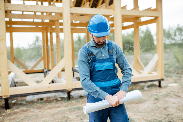 Builder with blueprints near the wooden house on the construction site ...