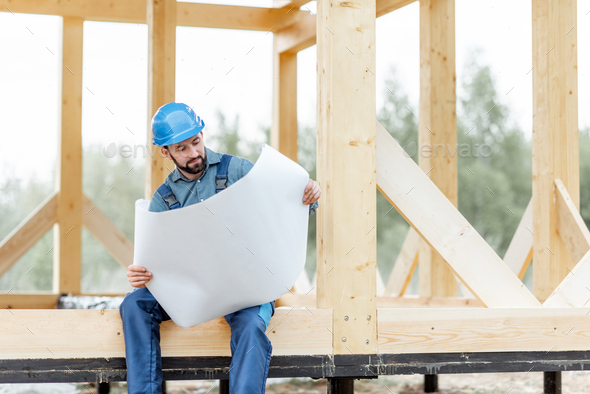 Builder with blueprints near the wooden house on the construction site ...