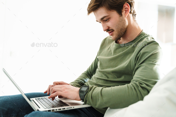 Photo of handsome young man typing on laptop while sitting Stock Photo ...