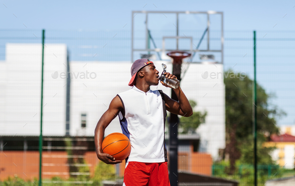 Young black basketball player drinking water to refresh himself after ...