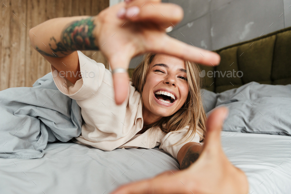 Image of woman making photo frame sign with fingers while lying in bed ...