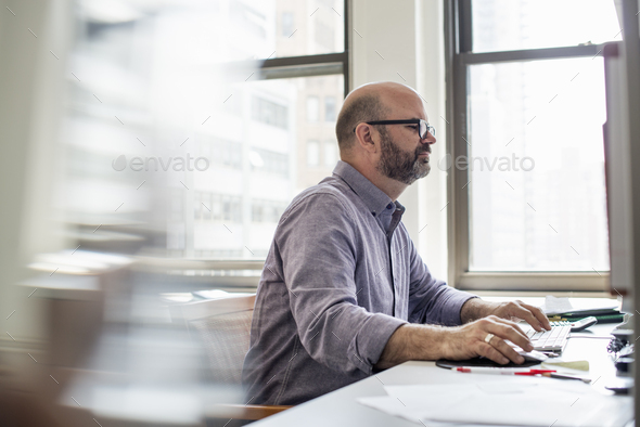 Office life. A man sitting at a desk using a computer, looking intently ...