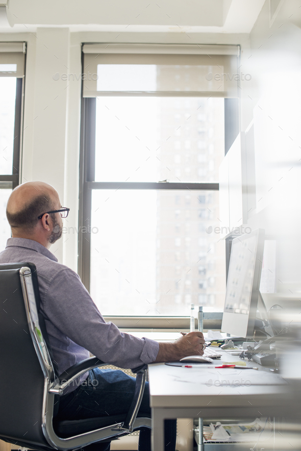 Office life. A man sitting at a desk using a computer, looking intently ...