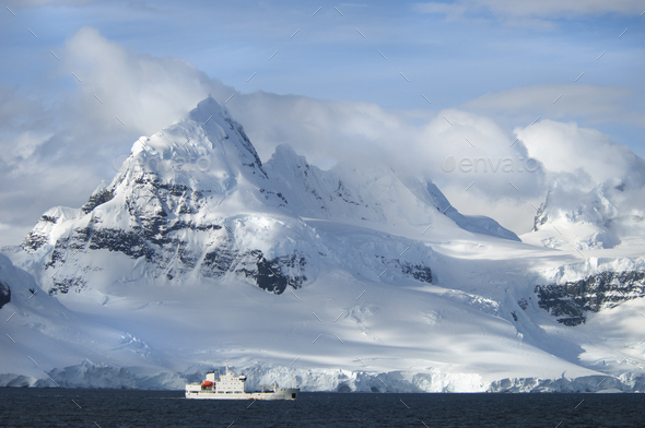 A ship under the towering shape of a mountain range. Stock Photo by ...