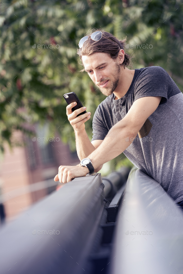 A young man leaning on a park railing checking his cell phone Stock ...