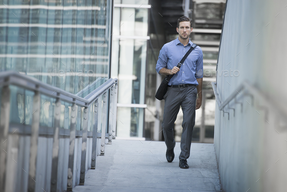 A man carrying a computer bag with a strap across his chest on along a ...
