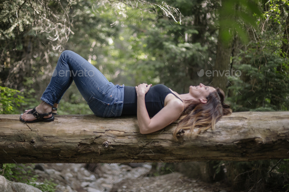 Woman lying on her back on a tree in a forest. Stock Photo by Mint_Images