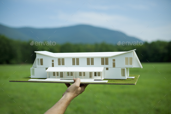 A rural scene and mountain range, and a person holding a scale model of ...