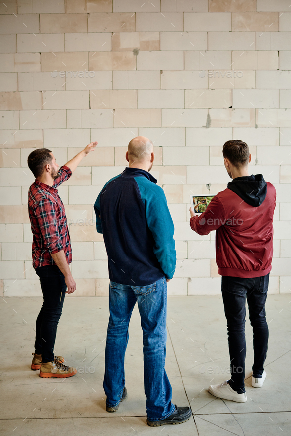 Back view of three young builders or architects discussing quality of ...