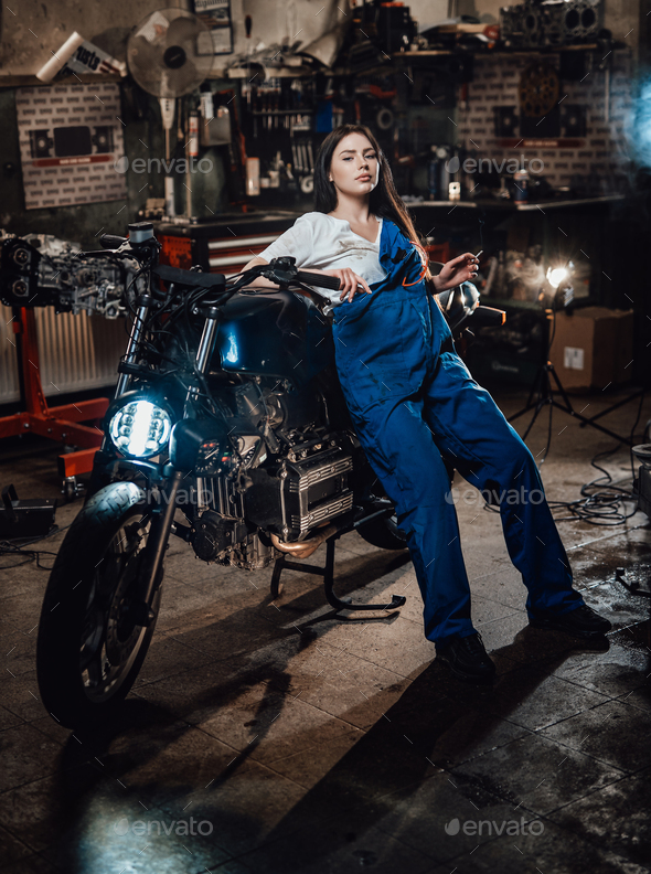 Female mechanic relaxing smoking a cigarette while leaning on custom ...