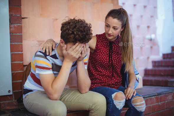 Schoolgirl sitting near staircase and consoling her sad friend Stock ...