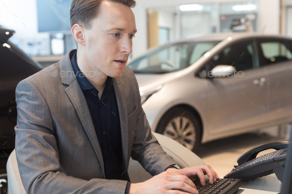 Salesman using computer in car showroom Stock Photo by Wavebreakmedia