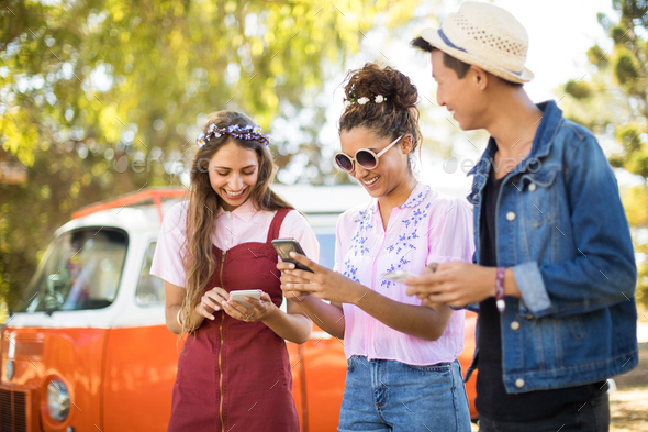 Smiling friends using phone while standing on field Stock Photo by ...