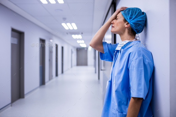 Sad surgeon leaning on wall in corridor Stock Photo by Wavebreakmedia