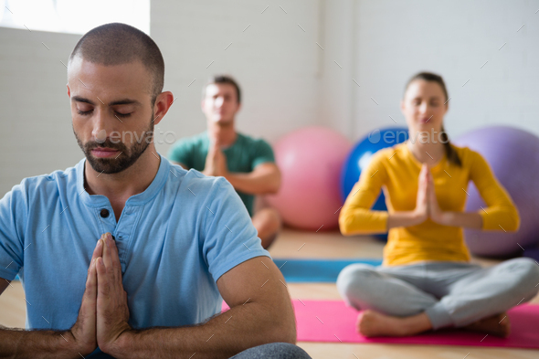 Yoga instructor with students meditating in prayer position at club ...