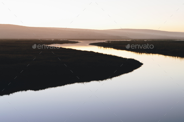 The open spaces of marshland and water channels. Flat calm water. Dusk ...