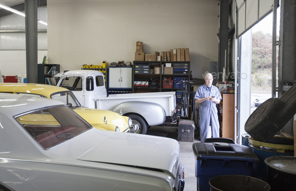 A mechanic standing in an auto repair shop, with a line of classic cars ...