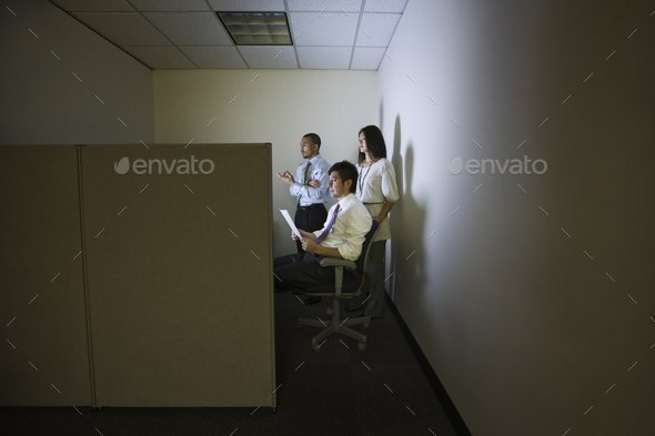 Three business people lit up by a desktop computer screen in a small ...
