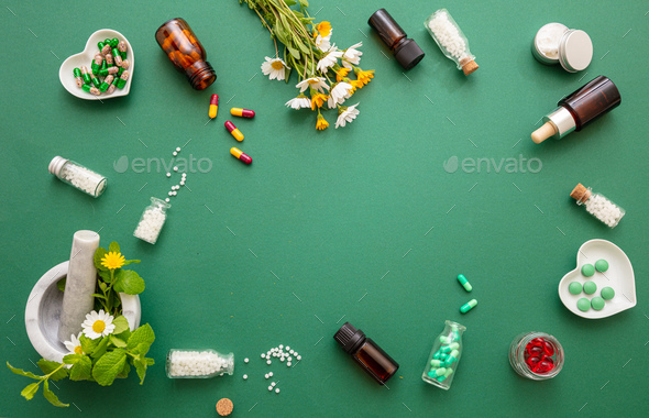Homeopathy, globules and herbs on green background Stock Photo by rawf8