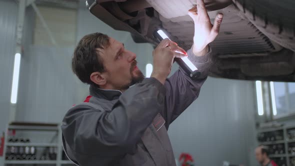 Man Auto Mechanic Looks Under the Car Raised on the Lift in Search of ...