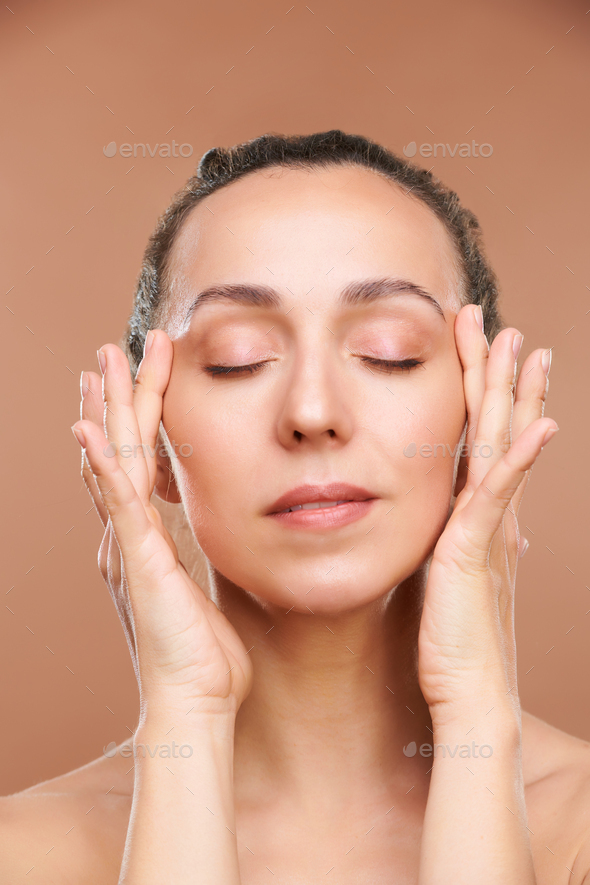 Pretty female with closed eyes touching eyelids while taking care of ...