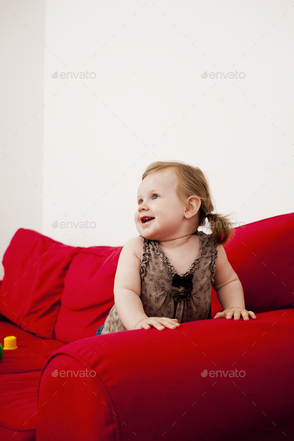 Cheerful baby girl sitting on red sofa at home Stock Photo by ...