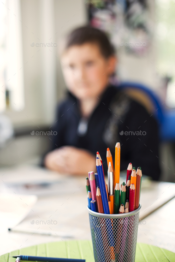 Colored pencils in container on desk with schoolboy in background at ...
